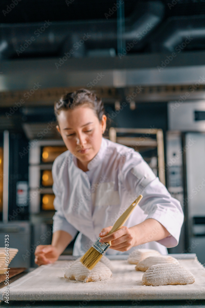 concentrated pretty woman baker smears raw bread rolls with egg before ...