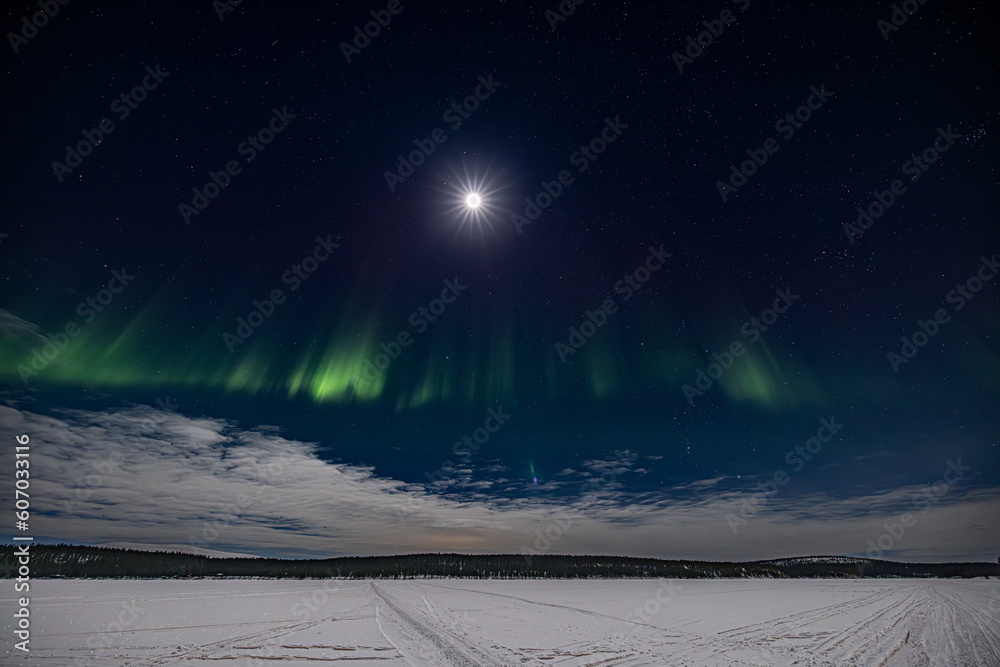 Green Northern lights (aurora borealis) with moon above Ounasjärvi lake ...