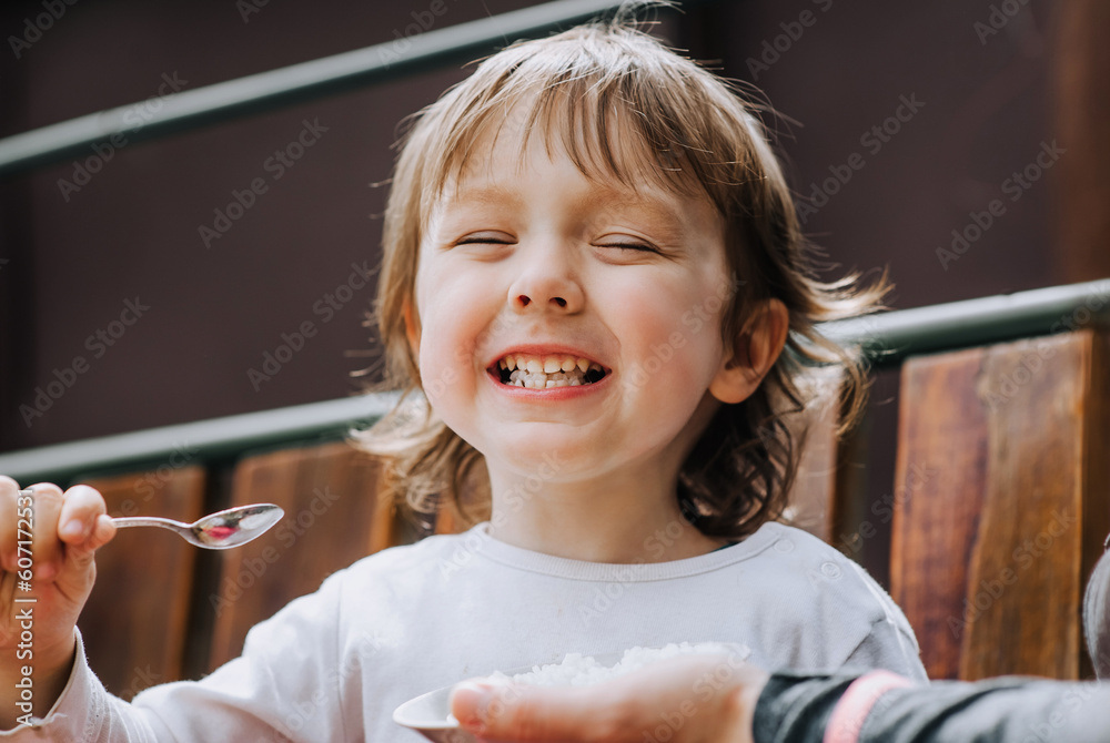 A beautiful little boy, a happy child, eats rice porridge with a spoon ...