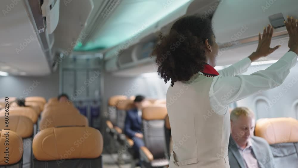 Woman flight attendant or air hostess closing and checking overhead ...
