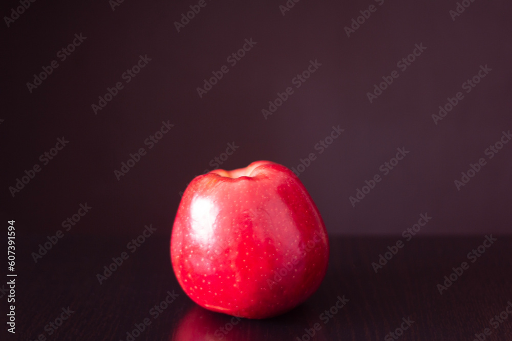 A red apple lies on a table against a dark background. Light from the ...