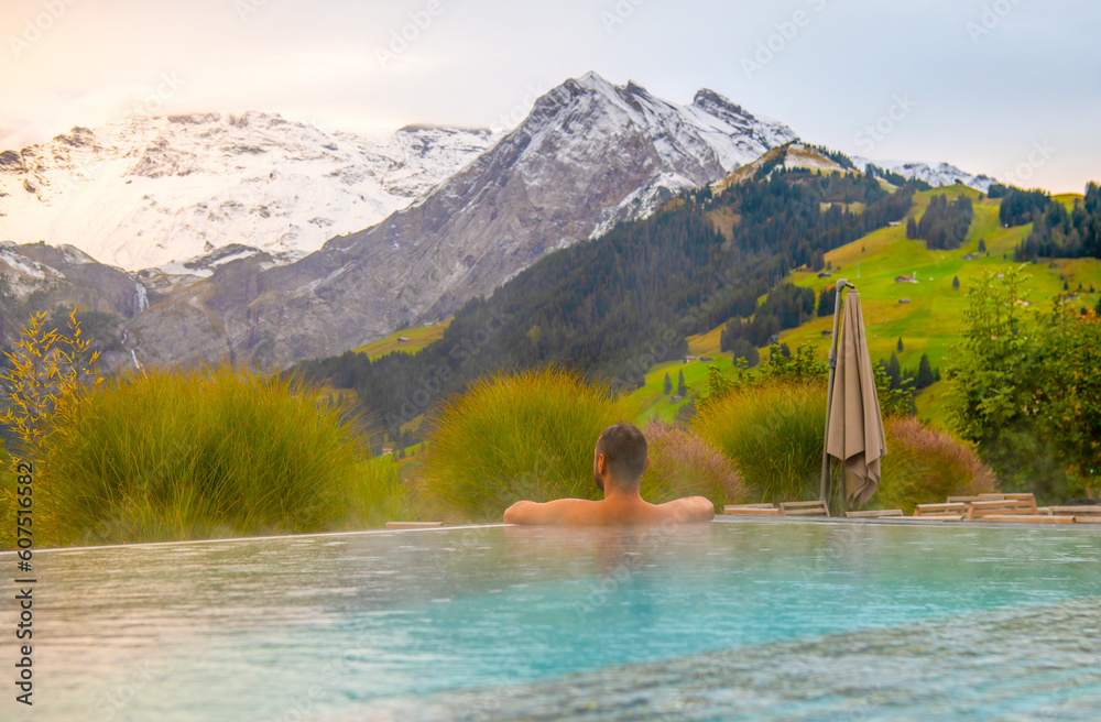 Man in outdoor infinity pool with snowy mountain in the background ...