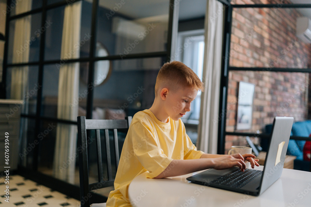 Side view of handsome 10 year old boy in yellow t-shirt typing on ...