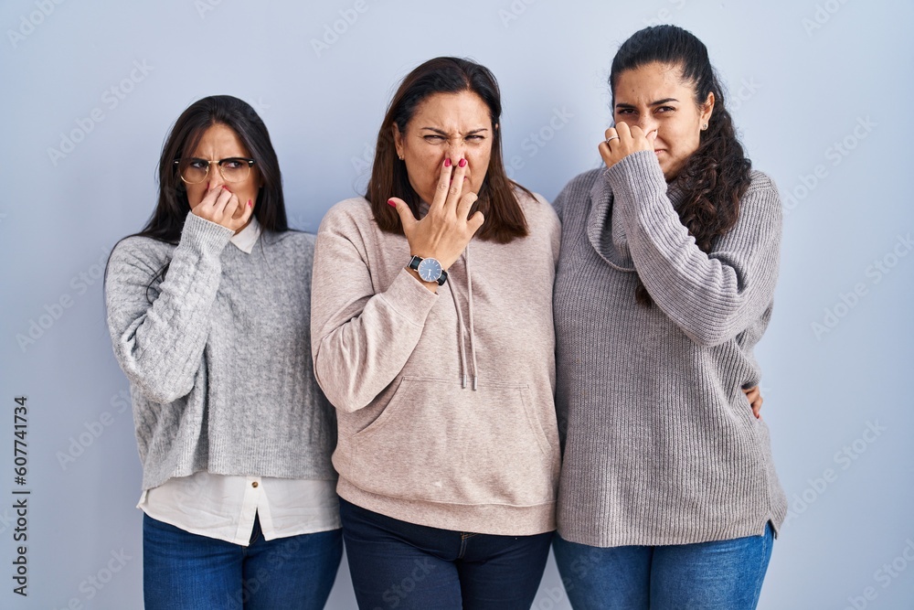 Mother and two daughters standing over blue background smelling ...