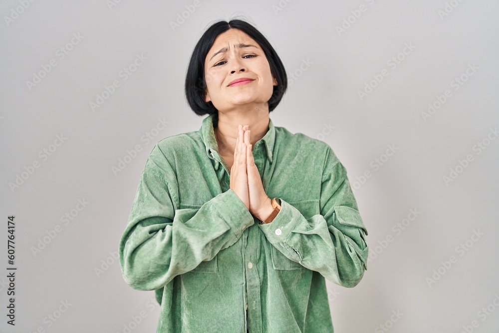 Young asian woman standing over white background begging and praying ...
