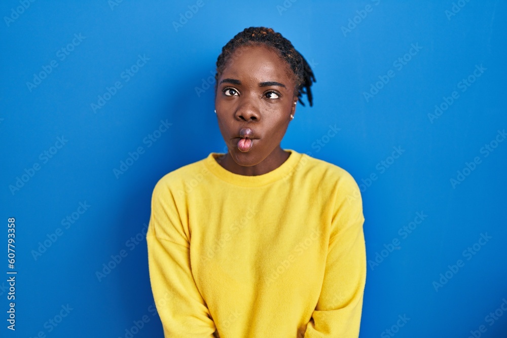 Beautiful black woman standing over blue background making fish face ...