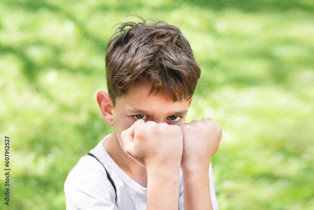 A young boy of 8 years old covers his face with his hands, fists, as if ...