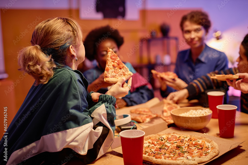 Side view portrait of young woman eating pizza with group of friends at ...