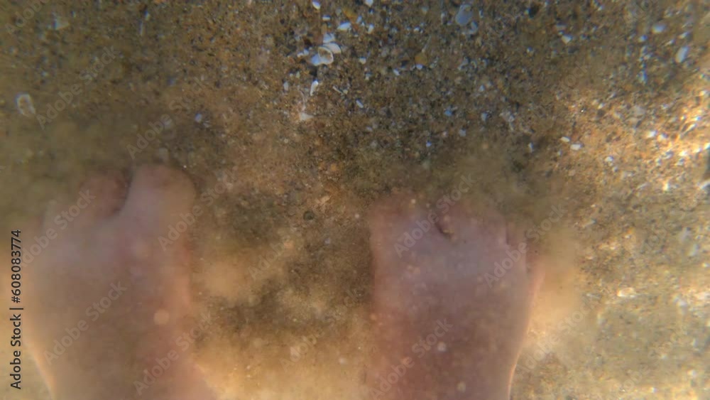 Woman standing barefoot on sand underwater and digging her feet into sand. Woman digging her ...