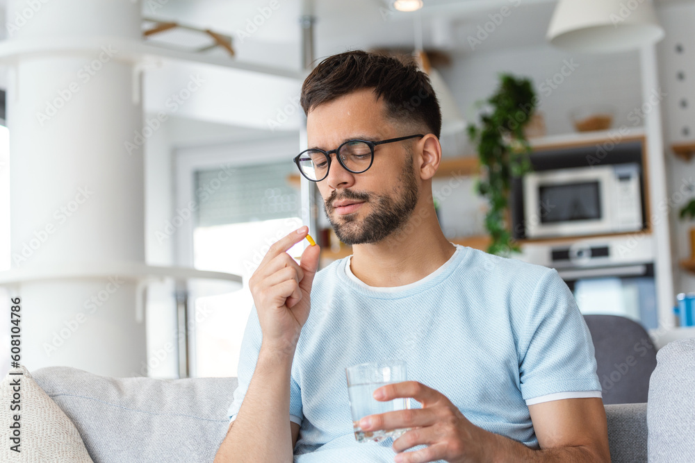 Young man takes medication prescribed by his physician. Man taking a pill and drinking a glass ...
