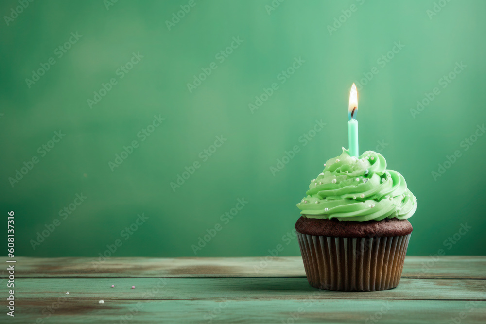 A green birthday party cupcake with one candle and confetti on blurred ...