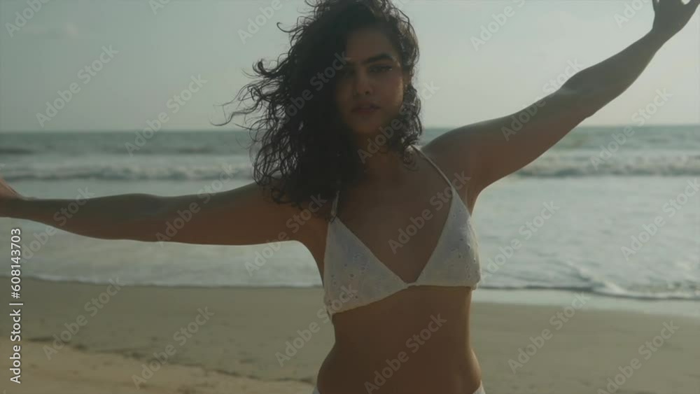 Beautiful Indian woman in a white bikini stretching on a white sandy beach. Have fun and relax ...
