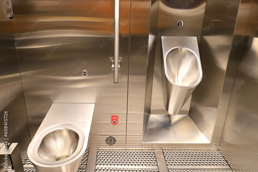 Plumbing metal urinal and toilet bowl in a public bathroom with ...