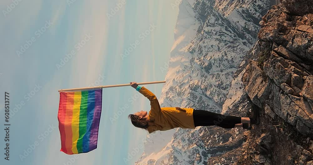 Side view of female in a mountain waving LGBT Pride flag. Woman holding ...