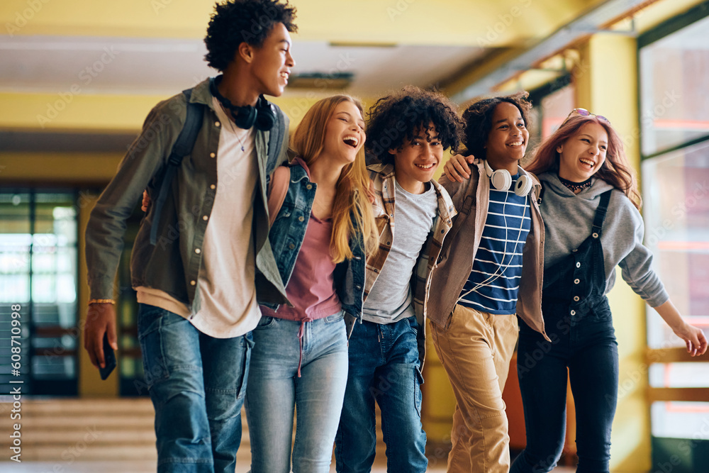 Multiracial group of cheerful high school friends walk through hallway ...