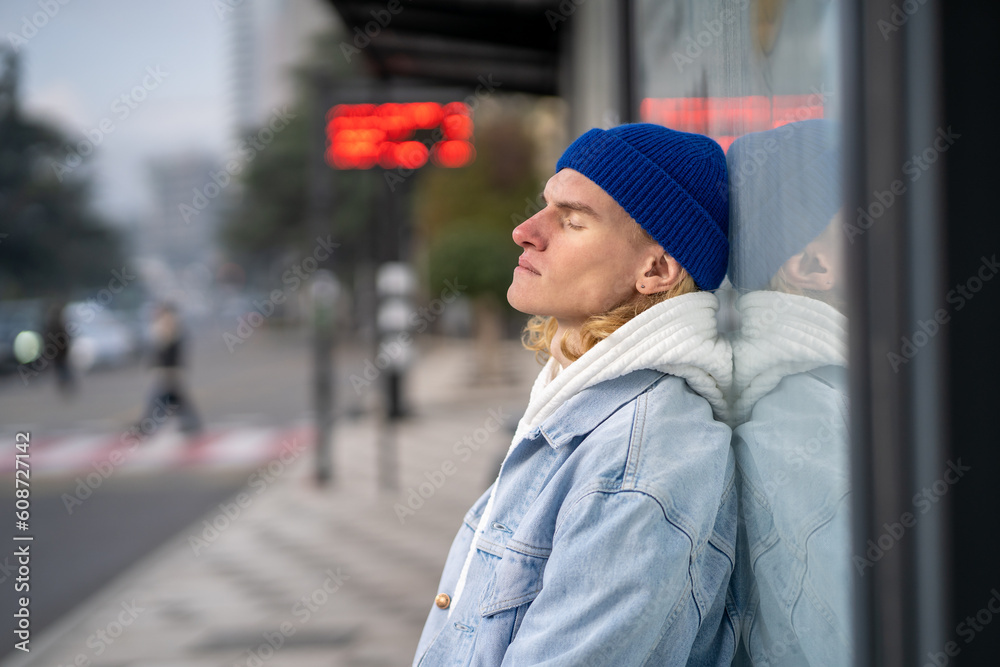 Tired hipster guy sitting with closed eyes at bus stop, feeling drained ...