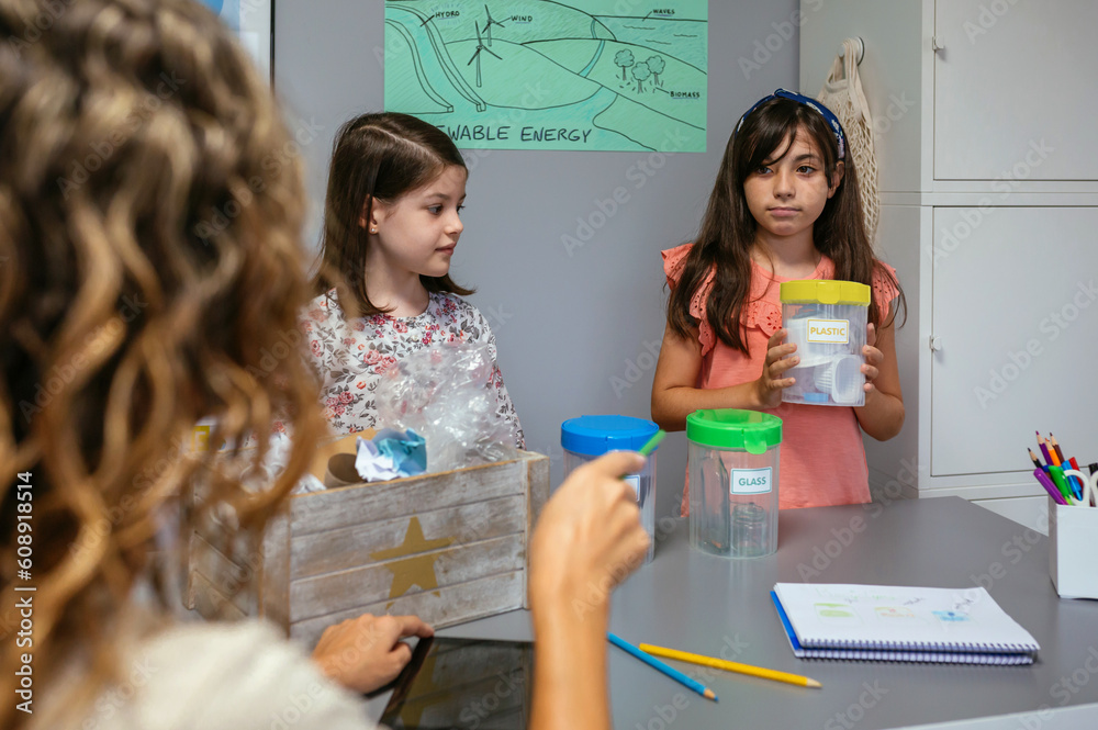 Girl student looking at teacher while holding sorting waste bin in ...