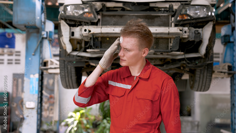 Caucasian male mechanic working in a garage, holding his head after ...