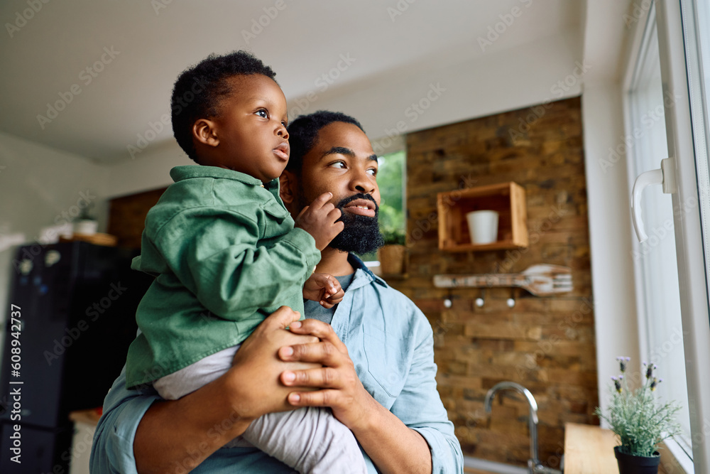 Black father holds his small son as they look out the window together ...