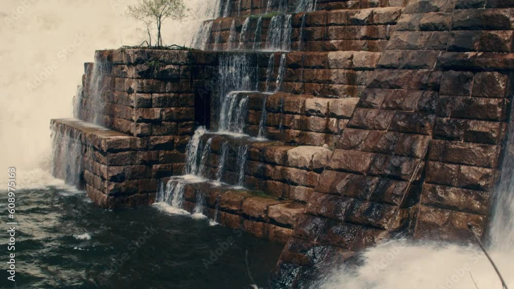 water falling down stepped spillway around small tree at the bottom of ...