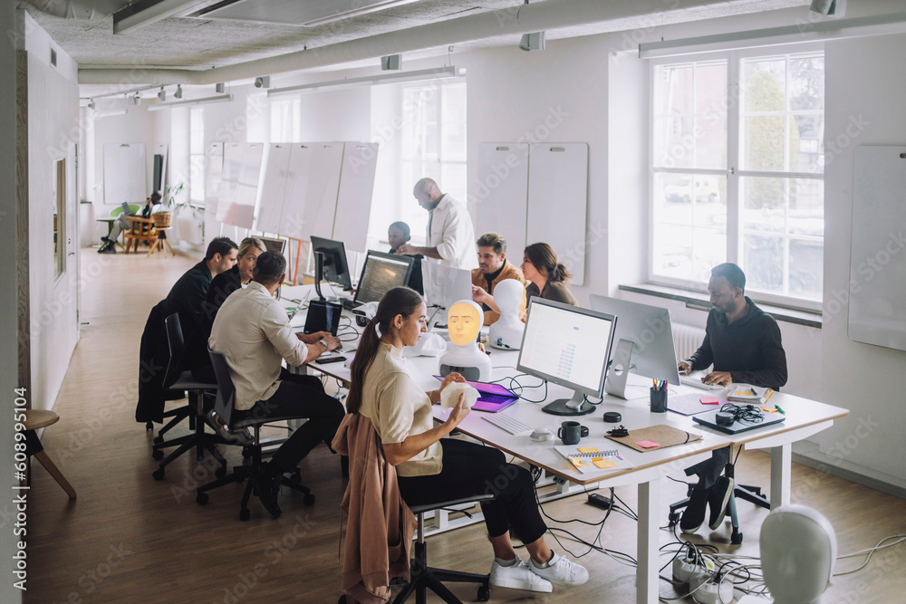 Professors discussing with PhD students over computer at desk in ...