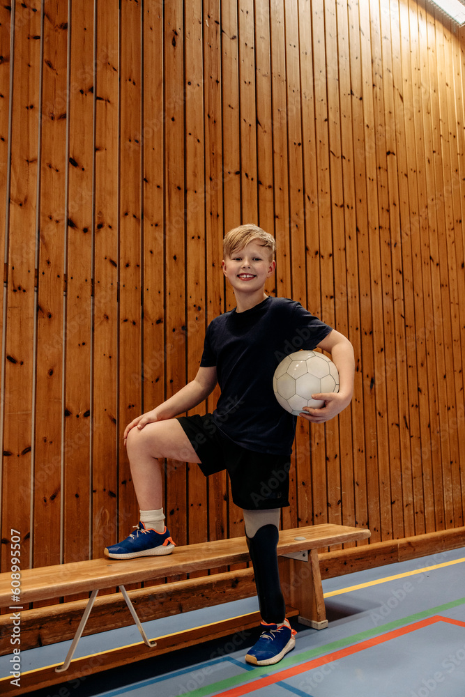 Smiling boy with amputated leg holding soccer ball while standing by ...