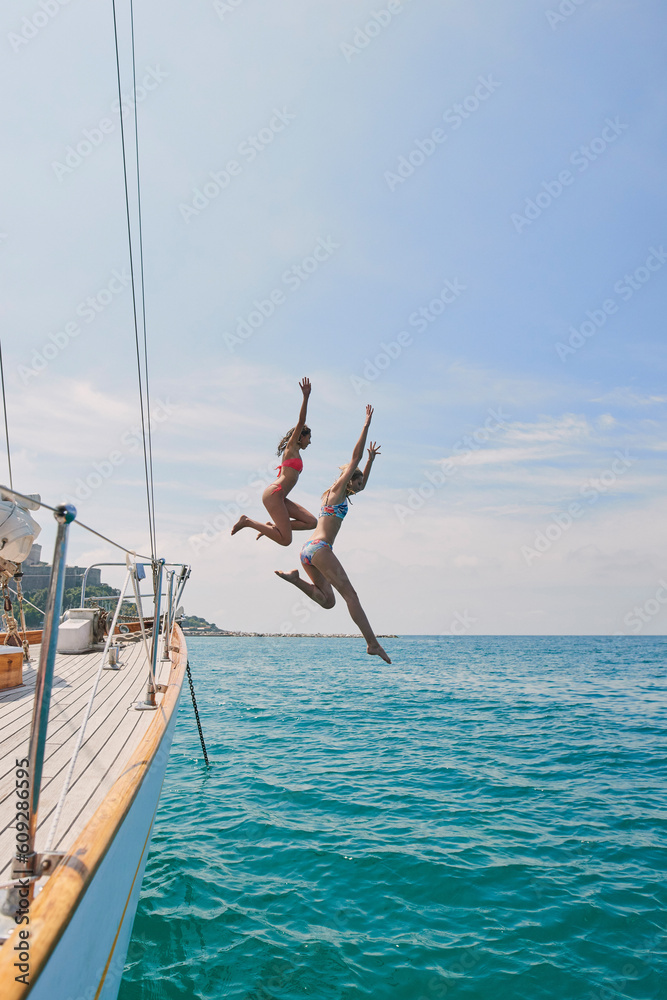 Summer, sailing and friends jumping off a yacht together into the ocean ...