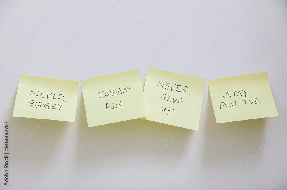 Four yellow sticky notes stuck across white wall with motivational and ...