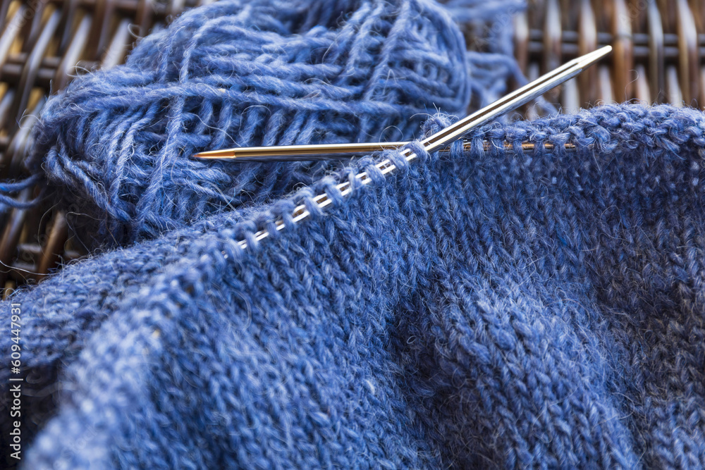 Blue wool yarn knitting on the metal needles with yarn ball ...