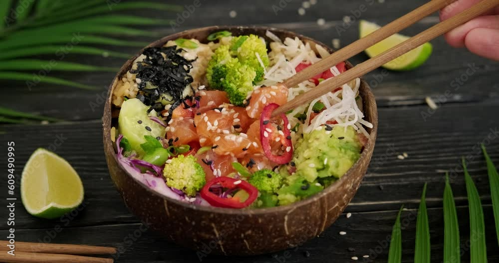 Person eating poke with chopsticks, taking a bite of salmon fish cubes ...