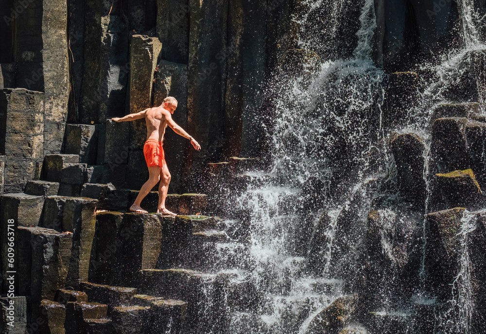 Caucasian man in swimsuit balancing near the falling water streams ...