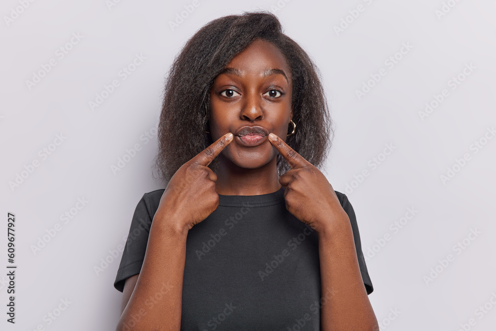 Indoor shot of pretty dark skinned woman points at corners of lips ...