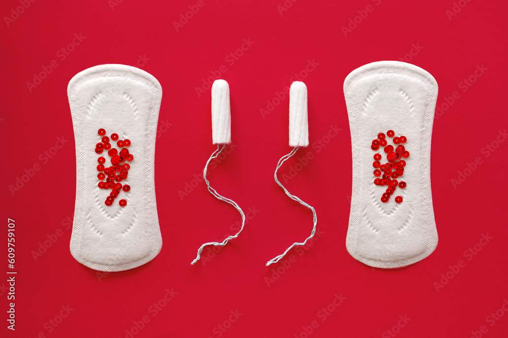Two menstrual tampons and two menstrual pads on a red background. The ...