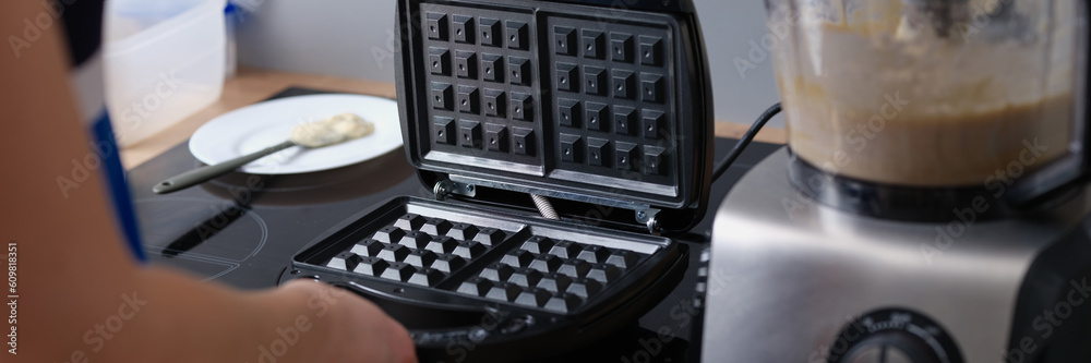 Woman opens waffle iron to make waffles in kitchen. Making waffles at ...
