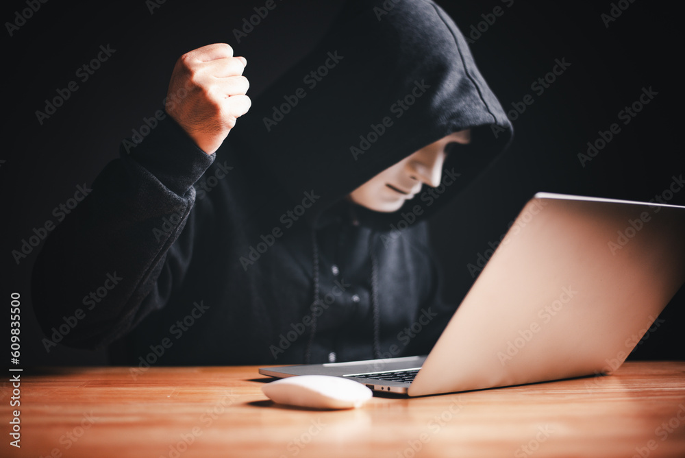 Black hat hacker punching the laptop computer screen display on table ...