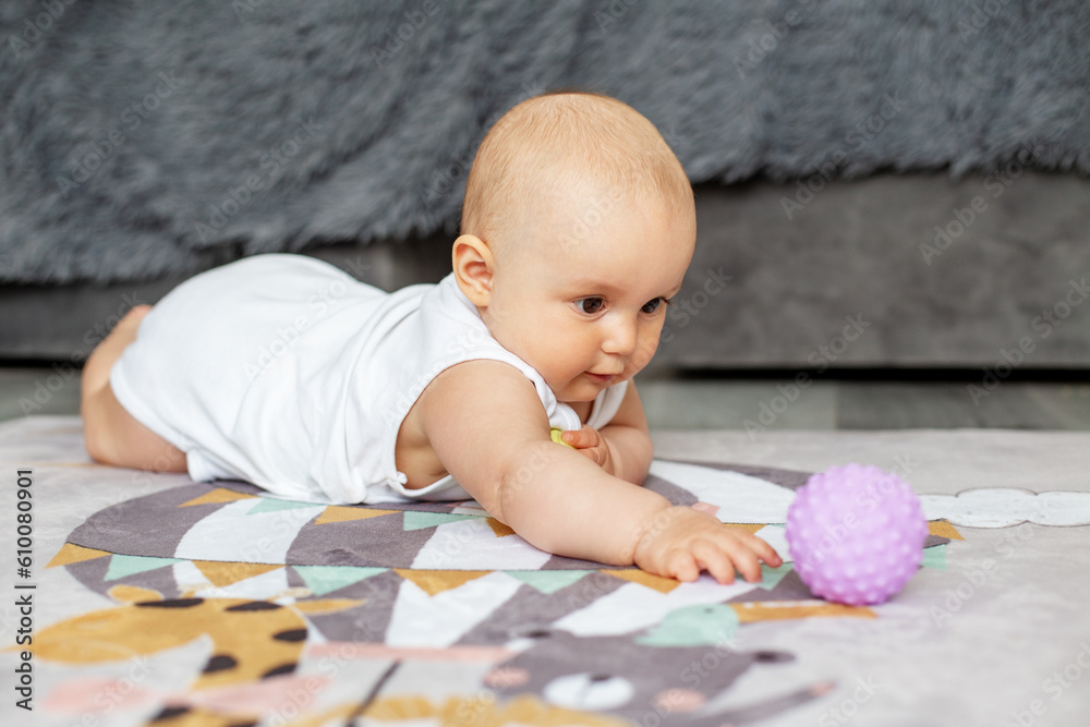 Baby creep on floor of nursery grabbing colorful ball. Baby development ...