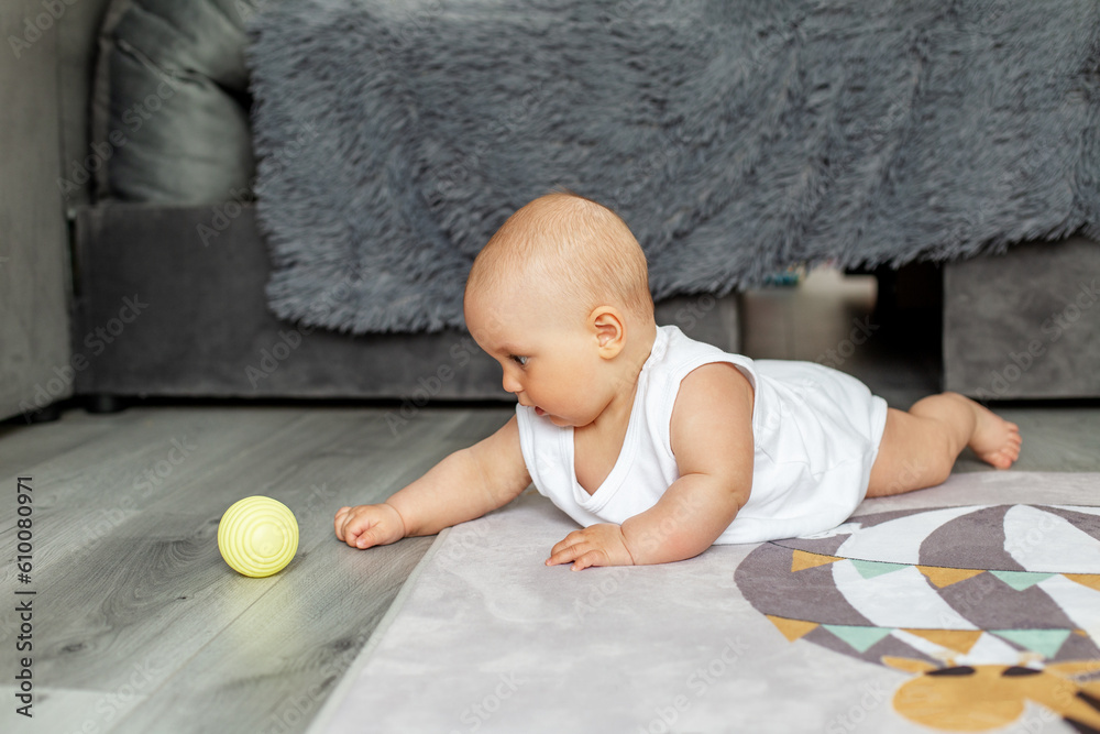 Baby creep on floor of nursery grabbing colorful ball. Baby development ...