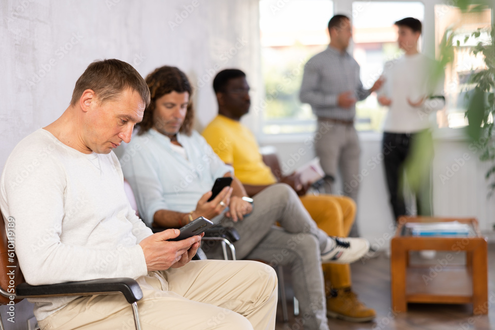 Serious man browsing websites on smartphone while sitting in lobby of ...