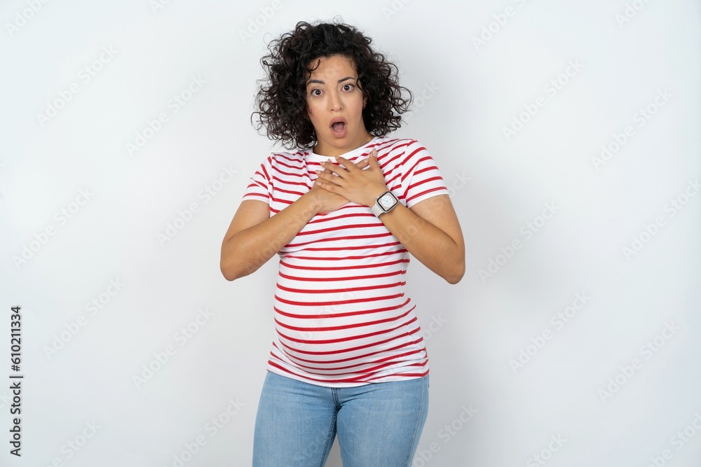 Scared young pregnant woman wearing striped t-shirt over white baclooks ...