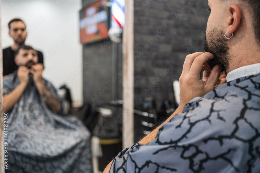 Barbershop customer reflected in the mirror touching his beard ...
