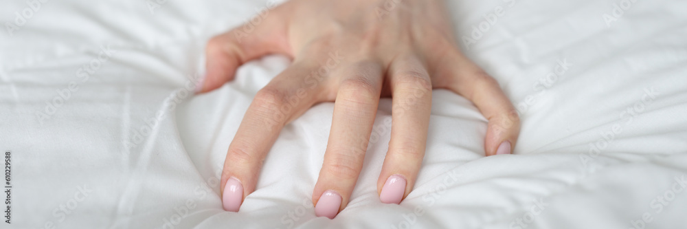 Strongly clenched female hand on sheet on bed. Intimacy of young woman ...