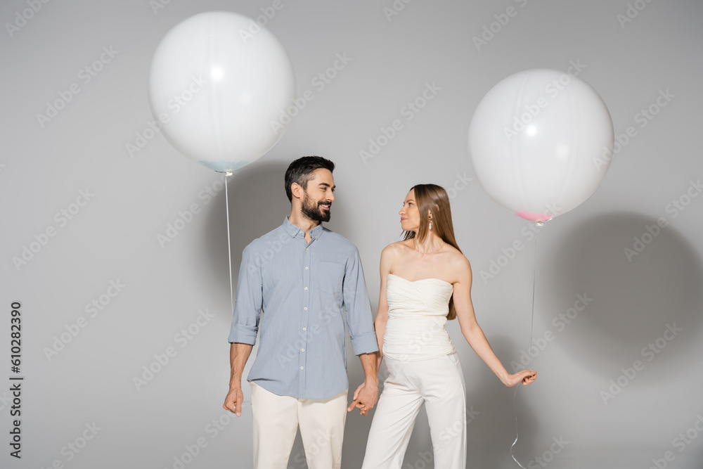 Positive and trendy expecting parents holding hands and festive ...