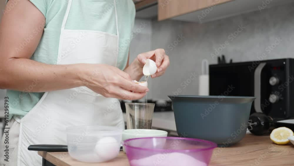 A woman is cooking in a bright kitchen. She cracks an egg and separates ...