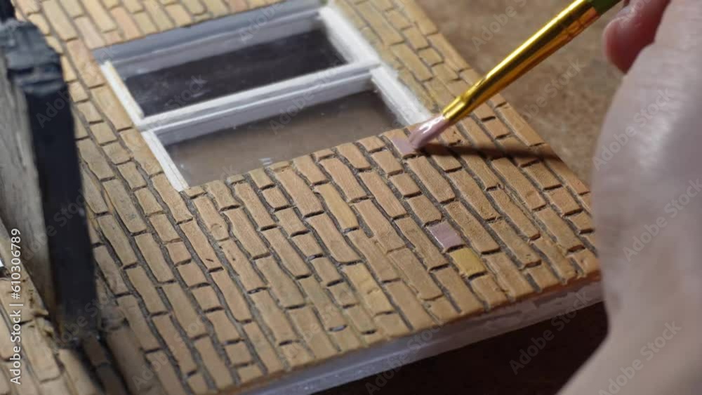 A miniature brick wall with a window is crafted by a master, who ...