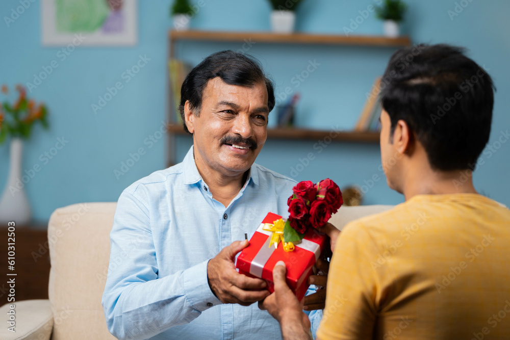 Happy senior father receiving gift with flowers from son at home ...