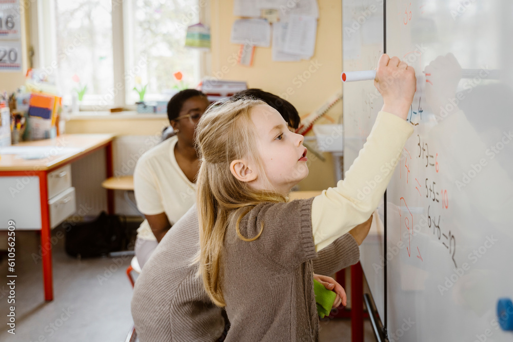 Blond girl solving maths problem while writing on whiteboard in ... Blond girl solving maths problem while writing on whiteboard in ...