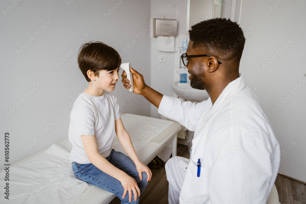 Young male pediatrician measuring temperature of boy using infrared ...