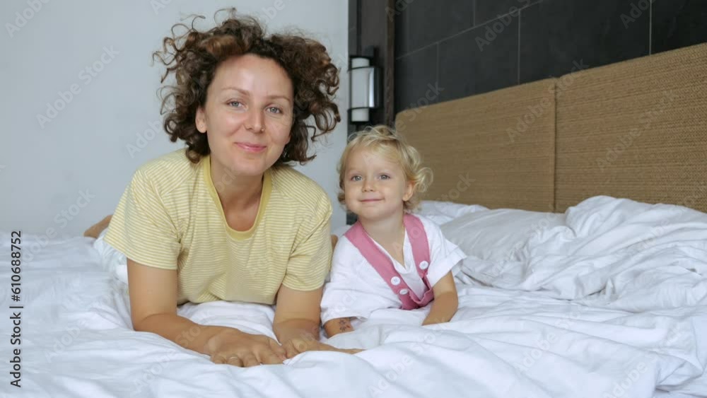 Attractive young curly-haired woman with cute little blonde girl lying ...