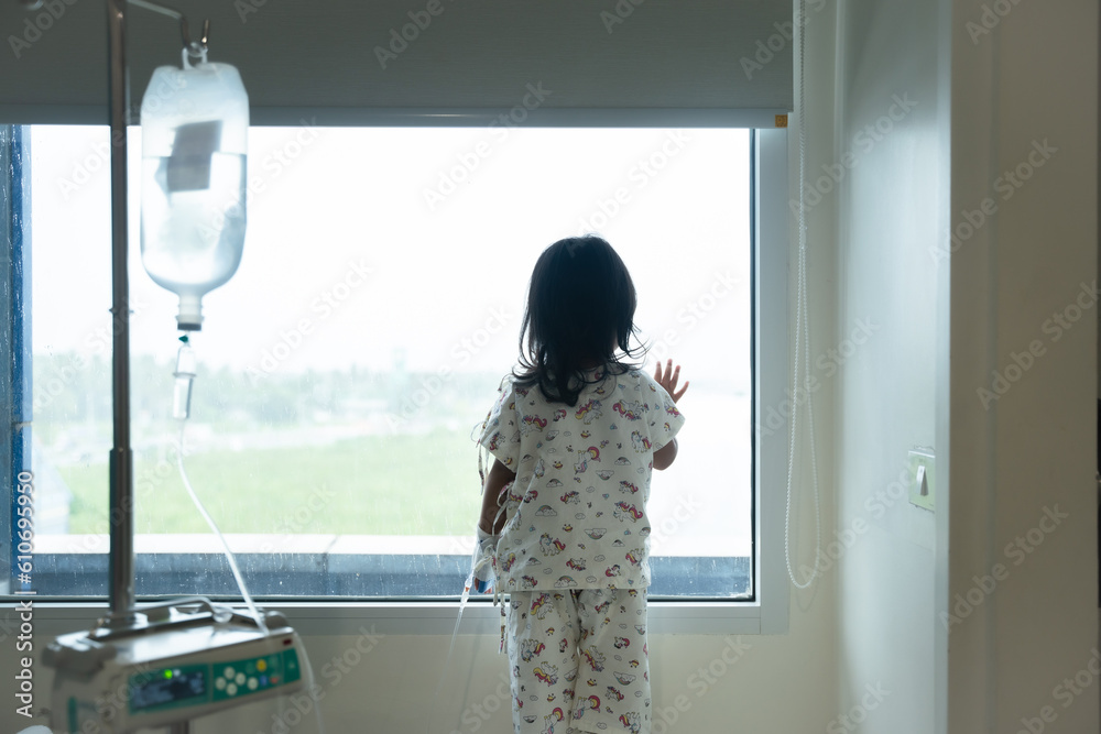 Child wearing IV tube is standing and looking out the window in ...