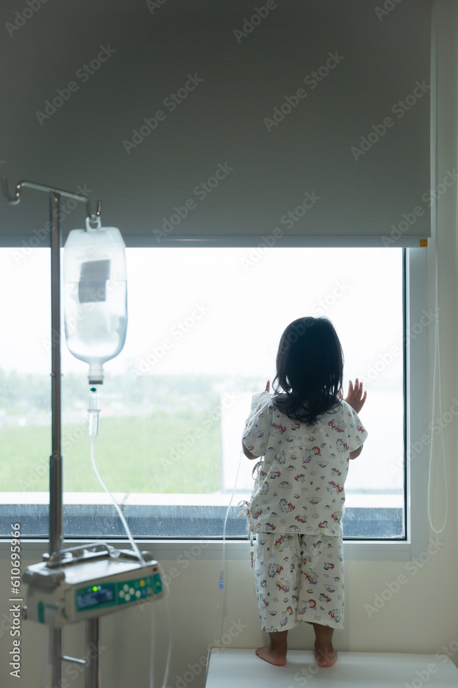 Child wearing IV tube is standing and looking out the window in ...